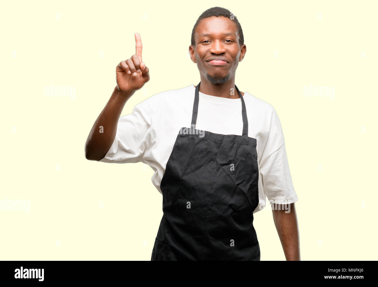 African man shop owner wearing apron raising finger, the number one ...