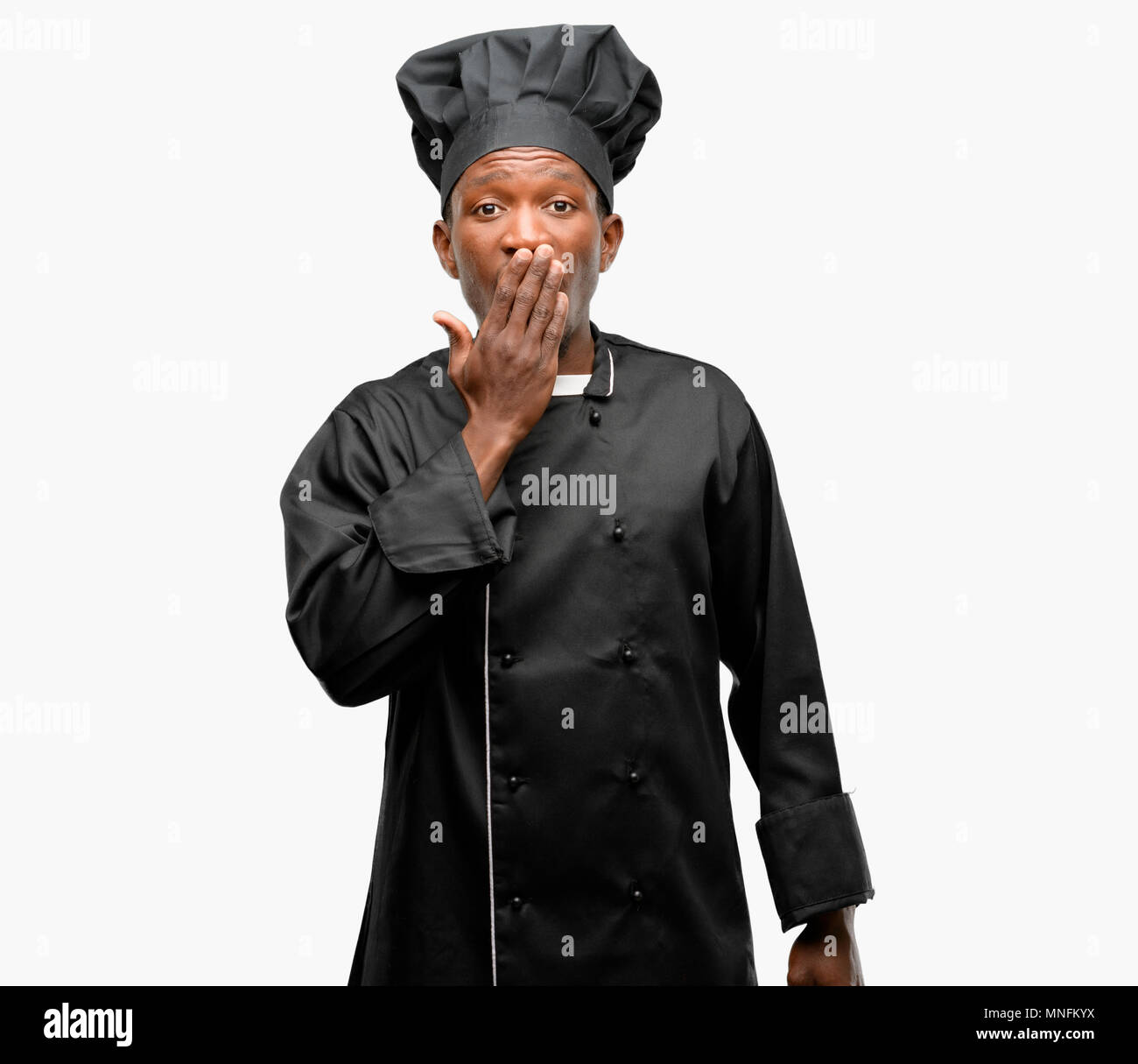 Young black cook wearing chef hat covers mouth in shock, looks shy ...
