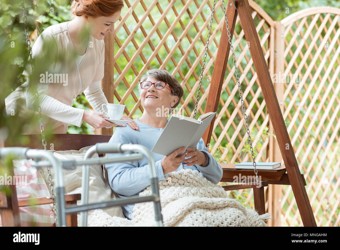 Smiling senior woman with glasses reading a book outside on garden ...