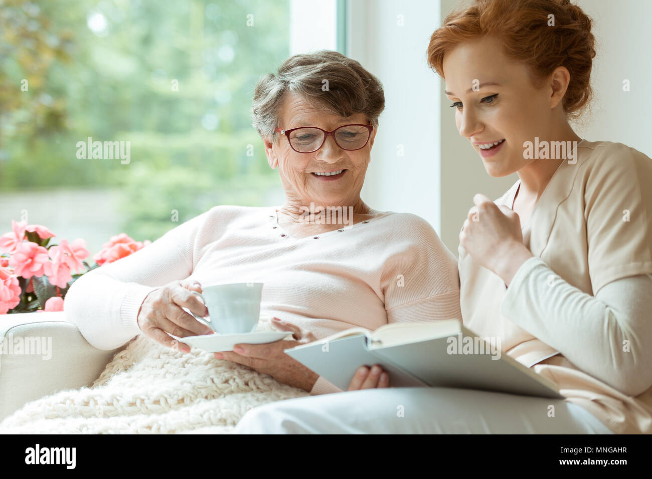 Smiling elder lady with blanket and glasses listening to her nurse ...