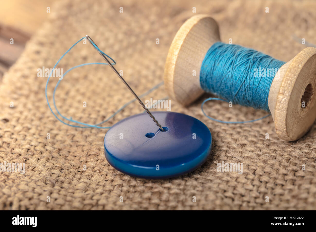 blue button with needle and thread close-up Stock Photo - Alamy