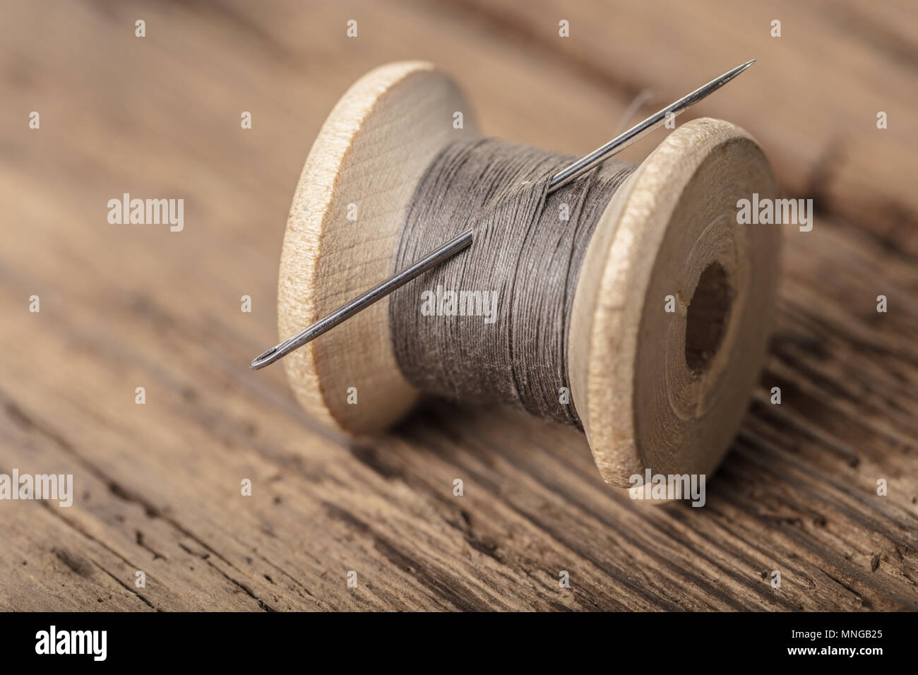 spool of thread with a needle on wooden background Stock Photo - Alamy