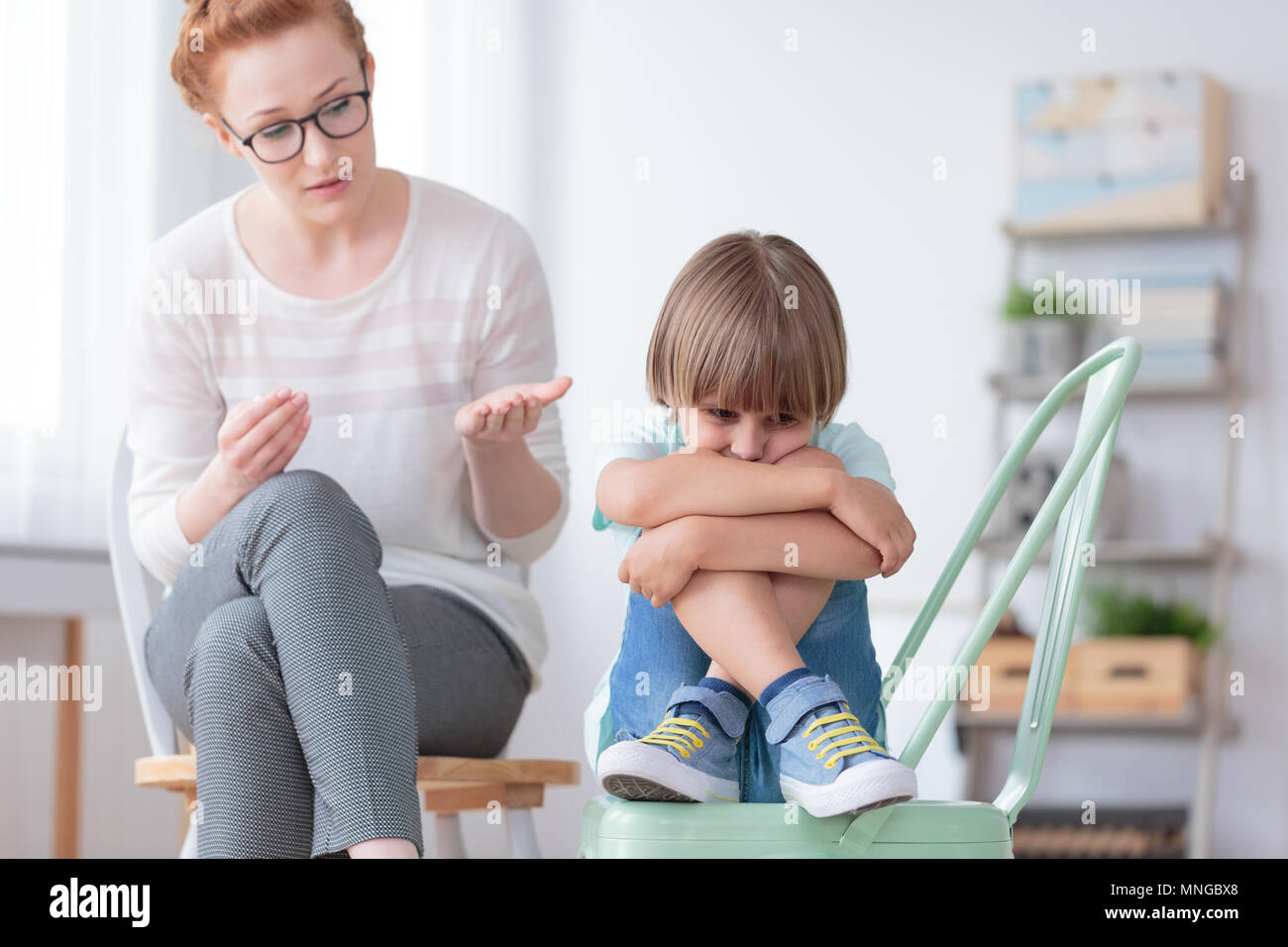 Worried autistic boy sitting with crossed legs on mint chair during ...