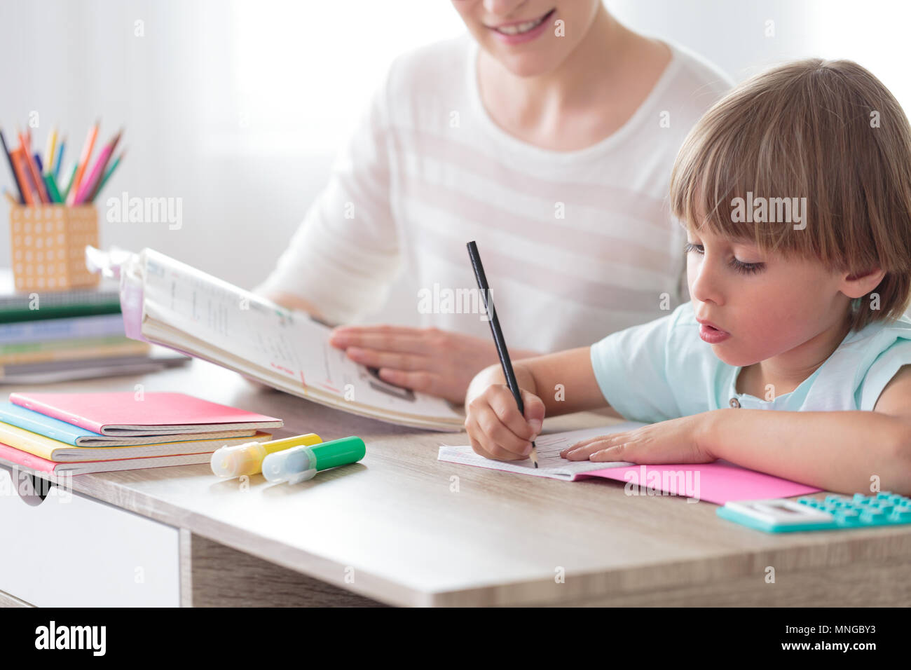 Boy focusing on his homework while sitting with mother at desk with ...