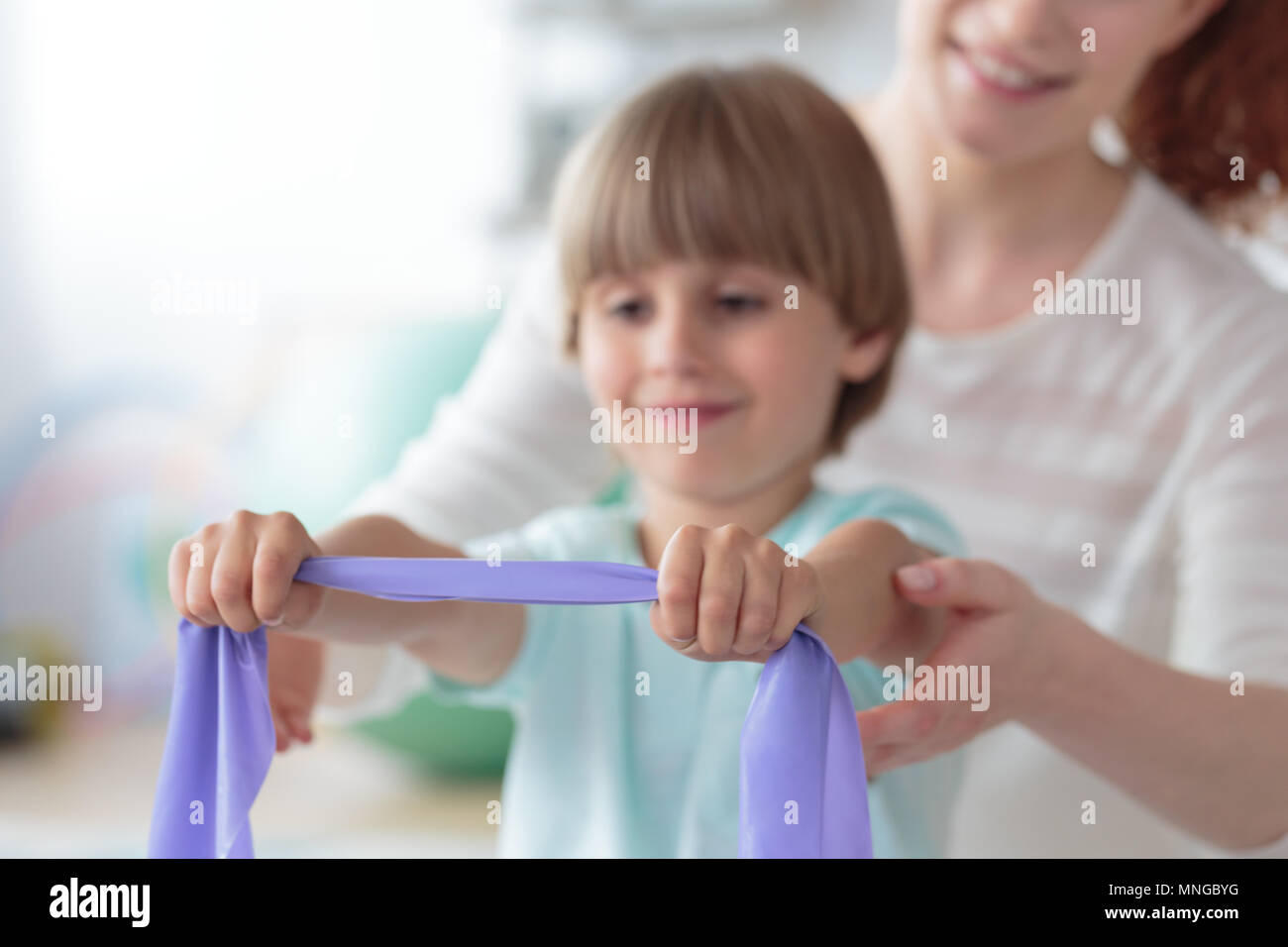 Physiotherapist supporting a young boy stretching with an elastic band ...