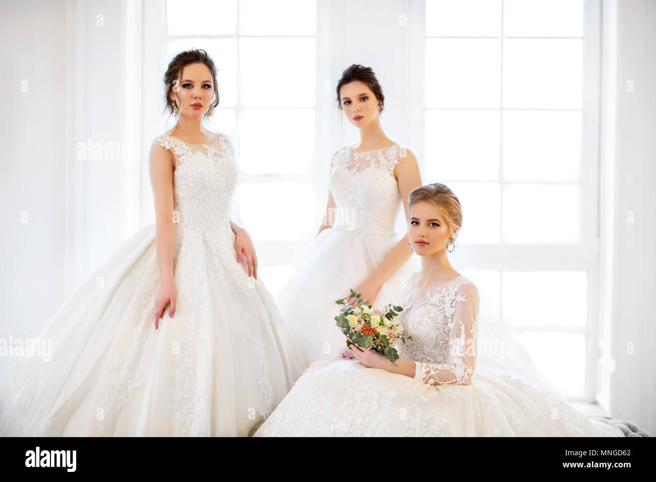 Three young woman with bouquets wearing wedding dresses Stock Photo - Alamy