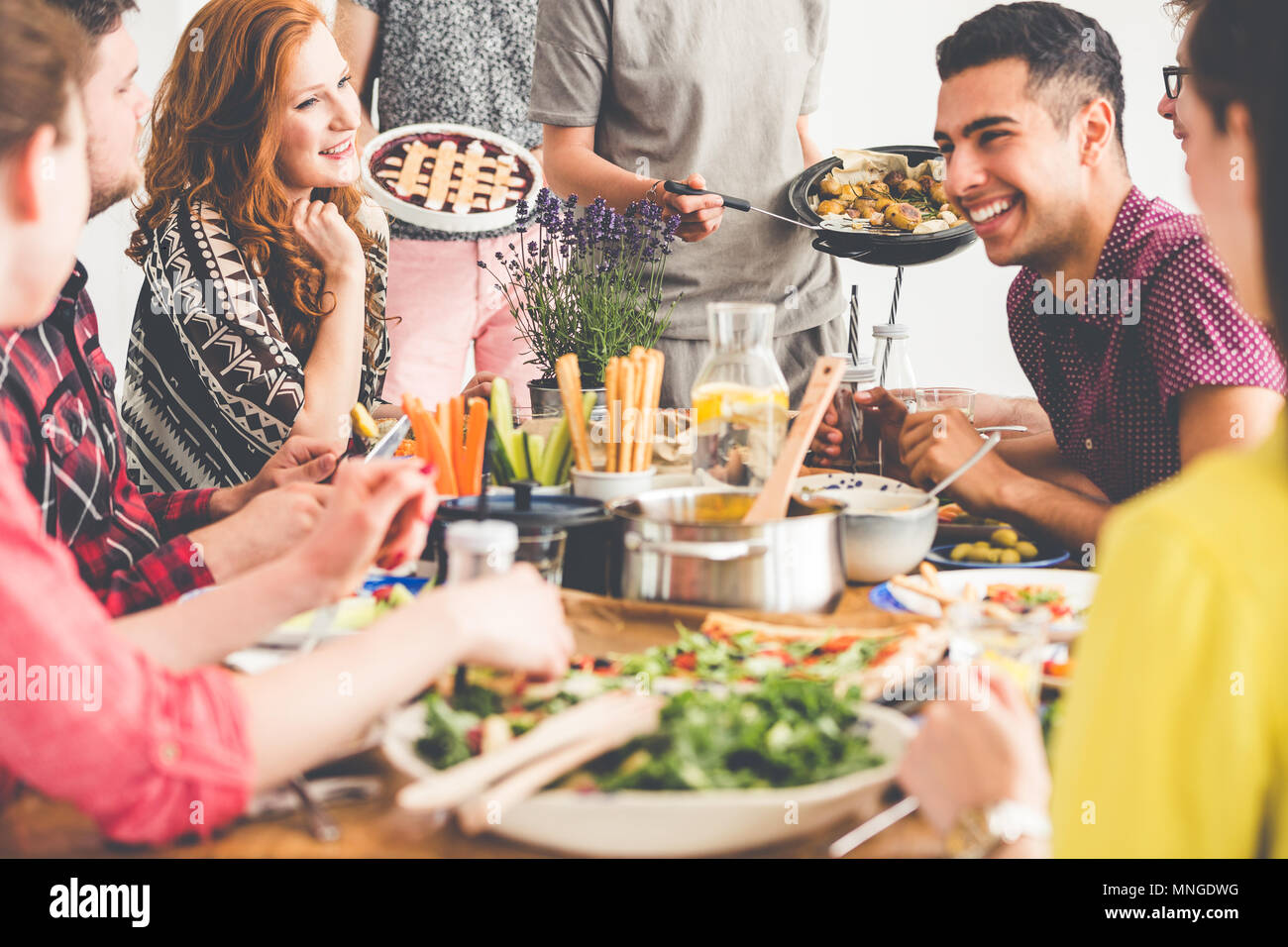 Healthy smiling friends enjoy meeting at communal table with hummus ...