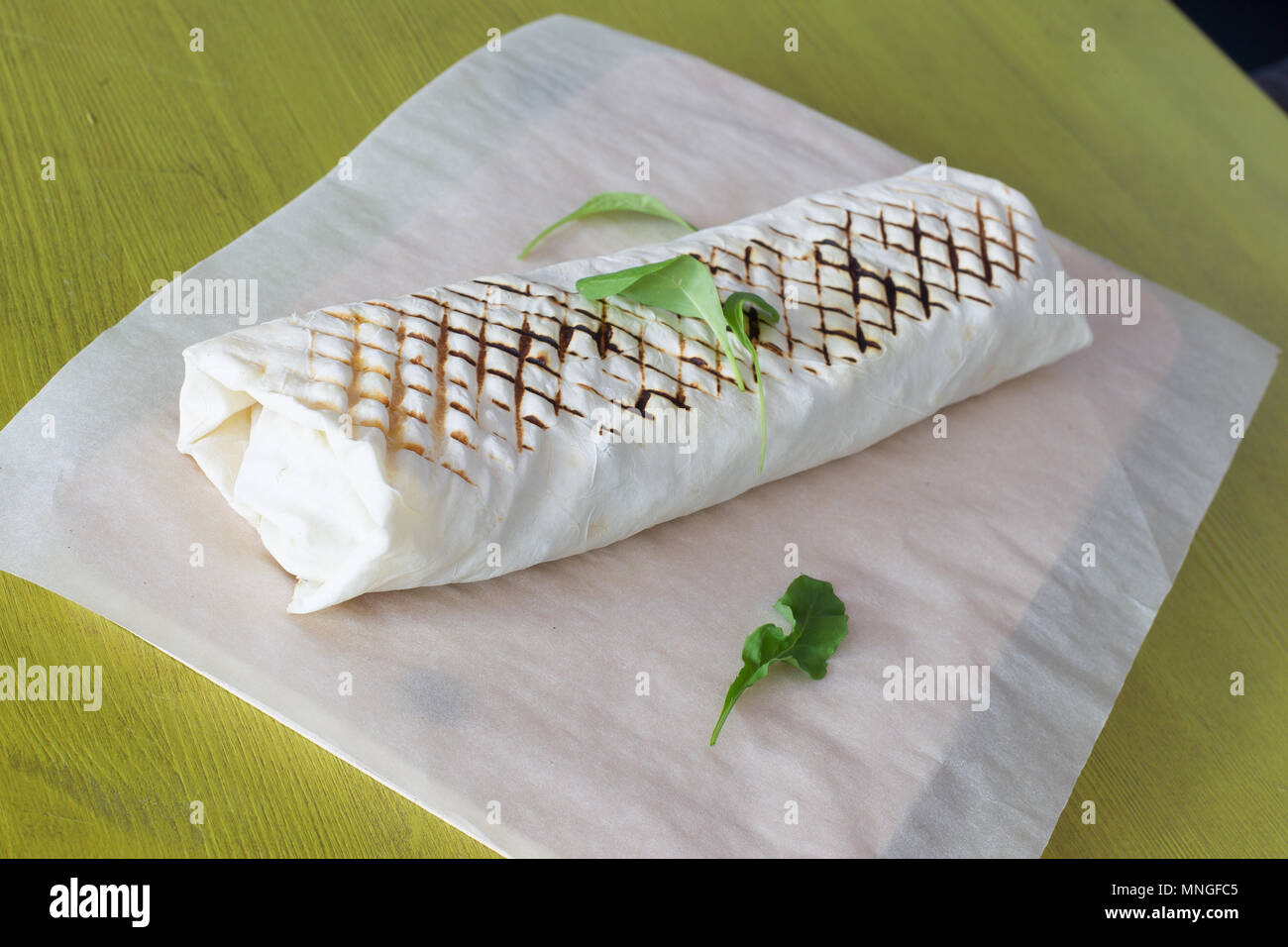 Roll of Armenian bread with meat and salad inside, laying on a table ...