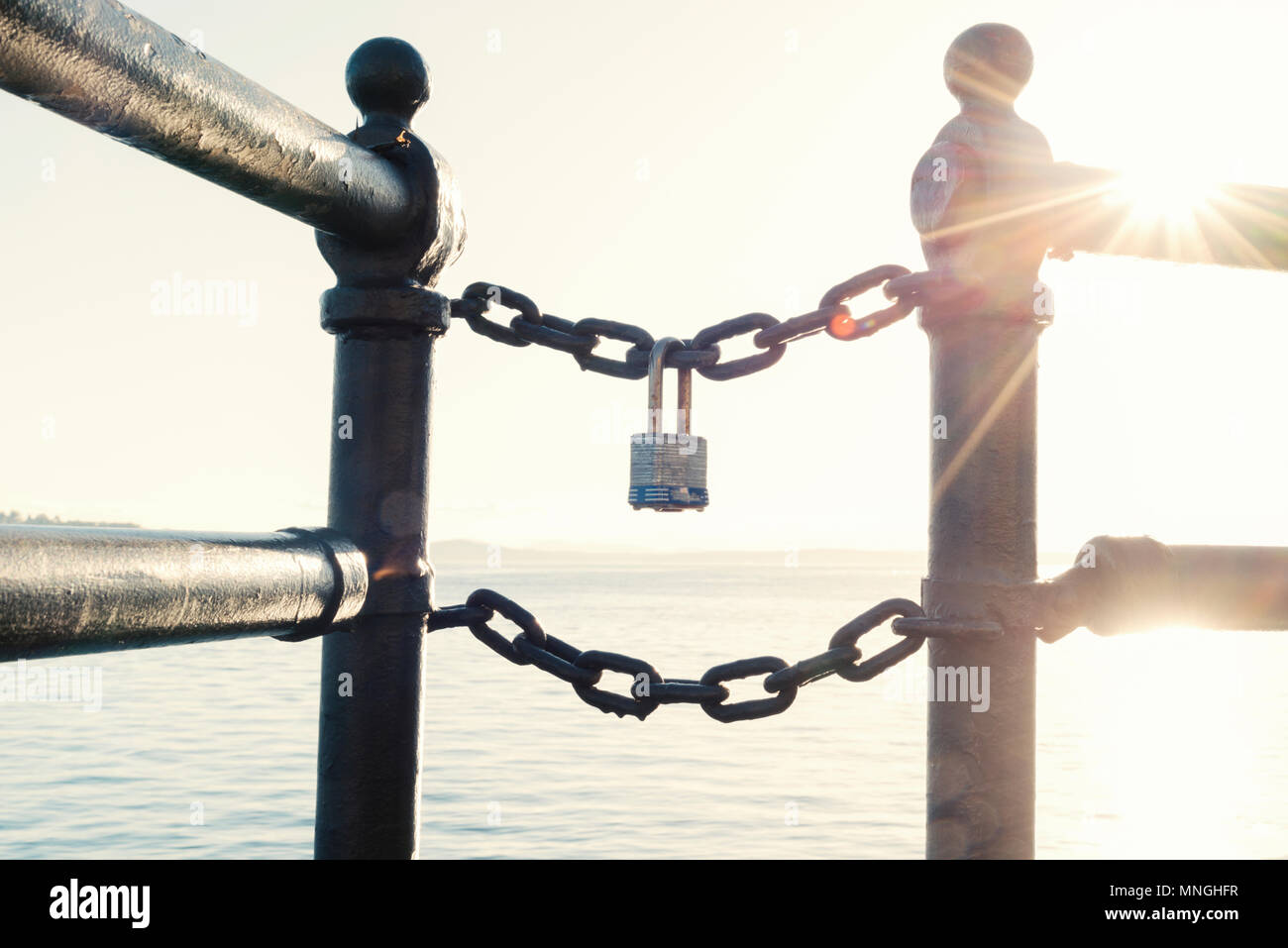 Steel lock locked to a chain with sunburst flare Stock Photo - Alamy