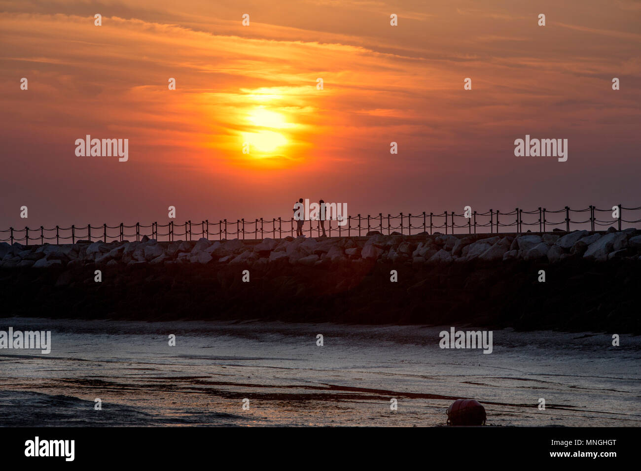 People talking on a harbour wall at sunset Stock Photo - Alamy