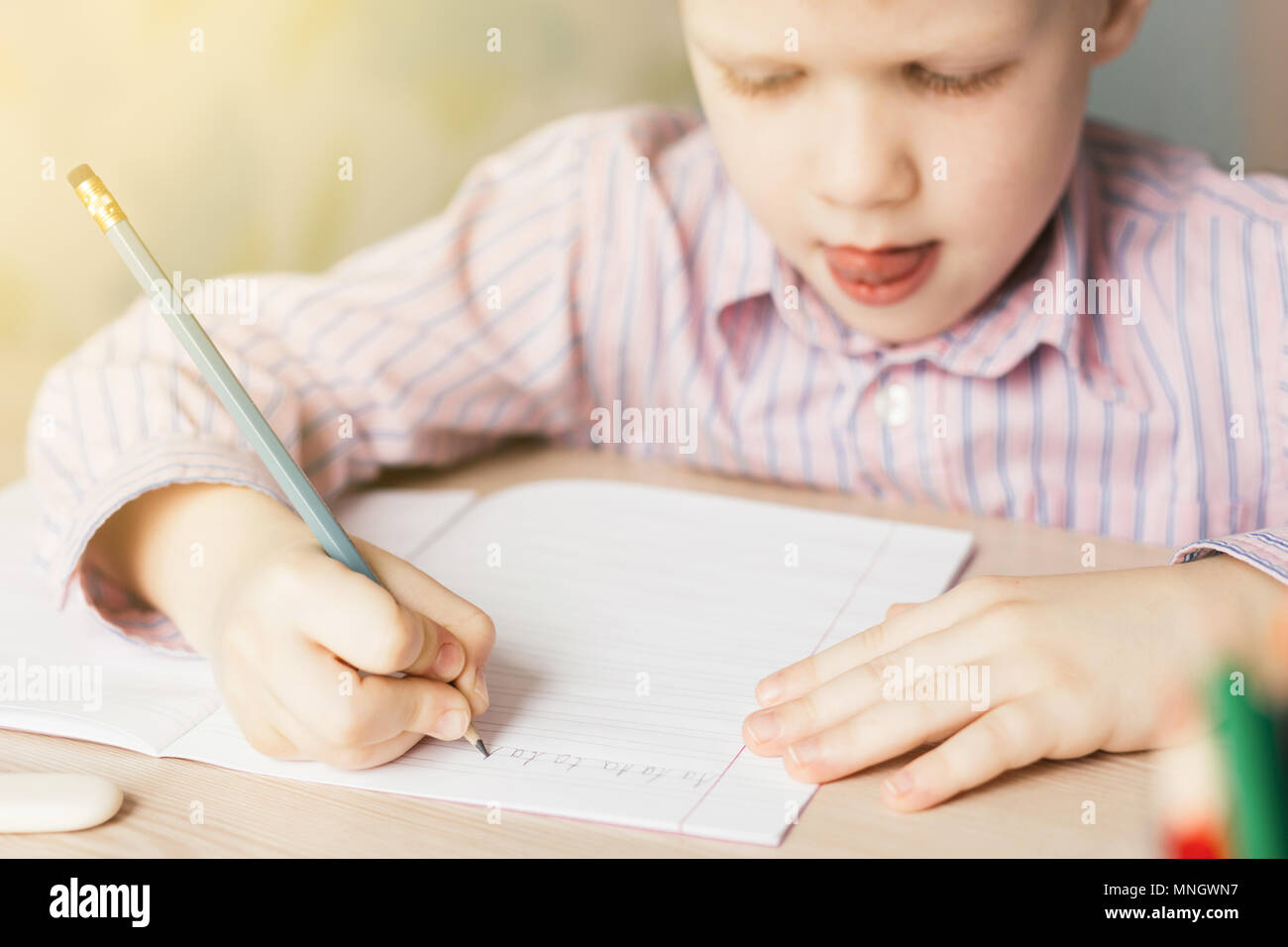 Cute little boy writing in notebook and sticking his tongue out. Kid ...