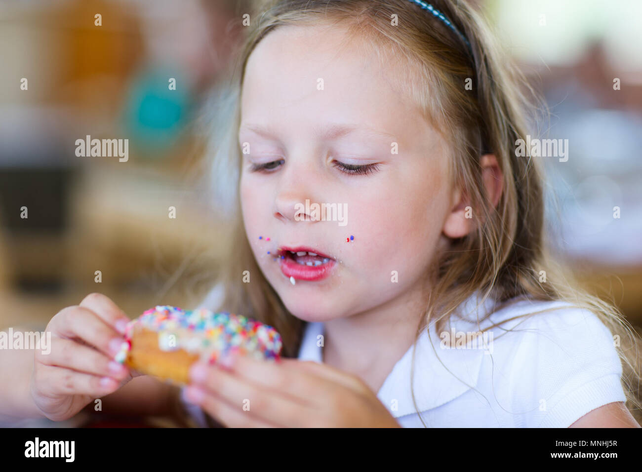 Adorable little girl enjoying eating donut at cafe Stock Photo - Alamy