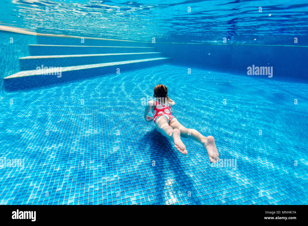 Underwater photo of adorable little girl diving and swimming in pool on ... Underwater photo of adorable little girl diving and swimming in pool on ...