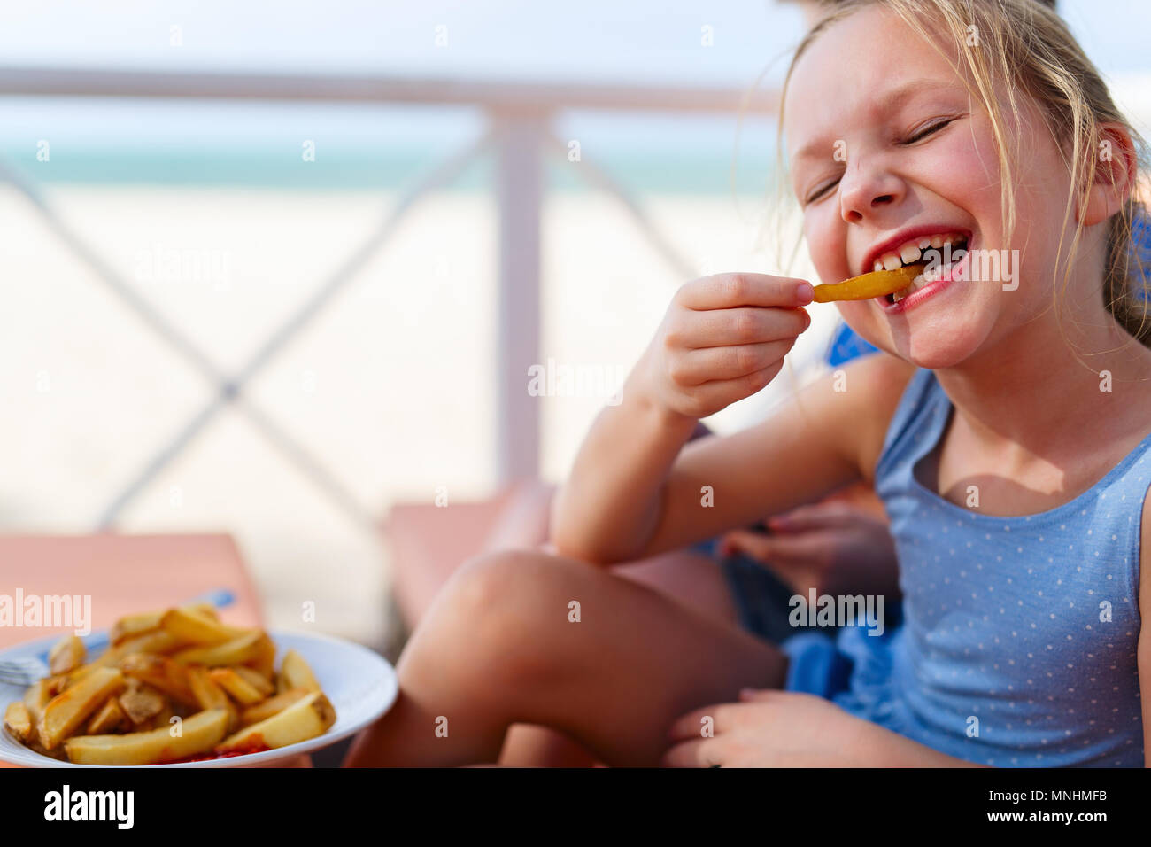 Adorable little girl enjoying eating french fries at outdoors ...