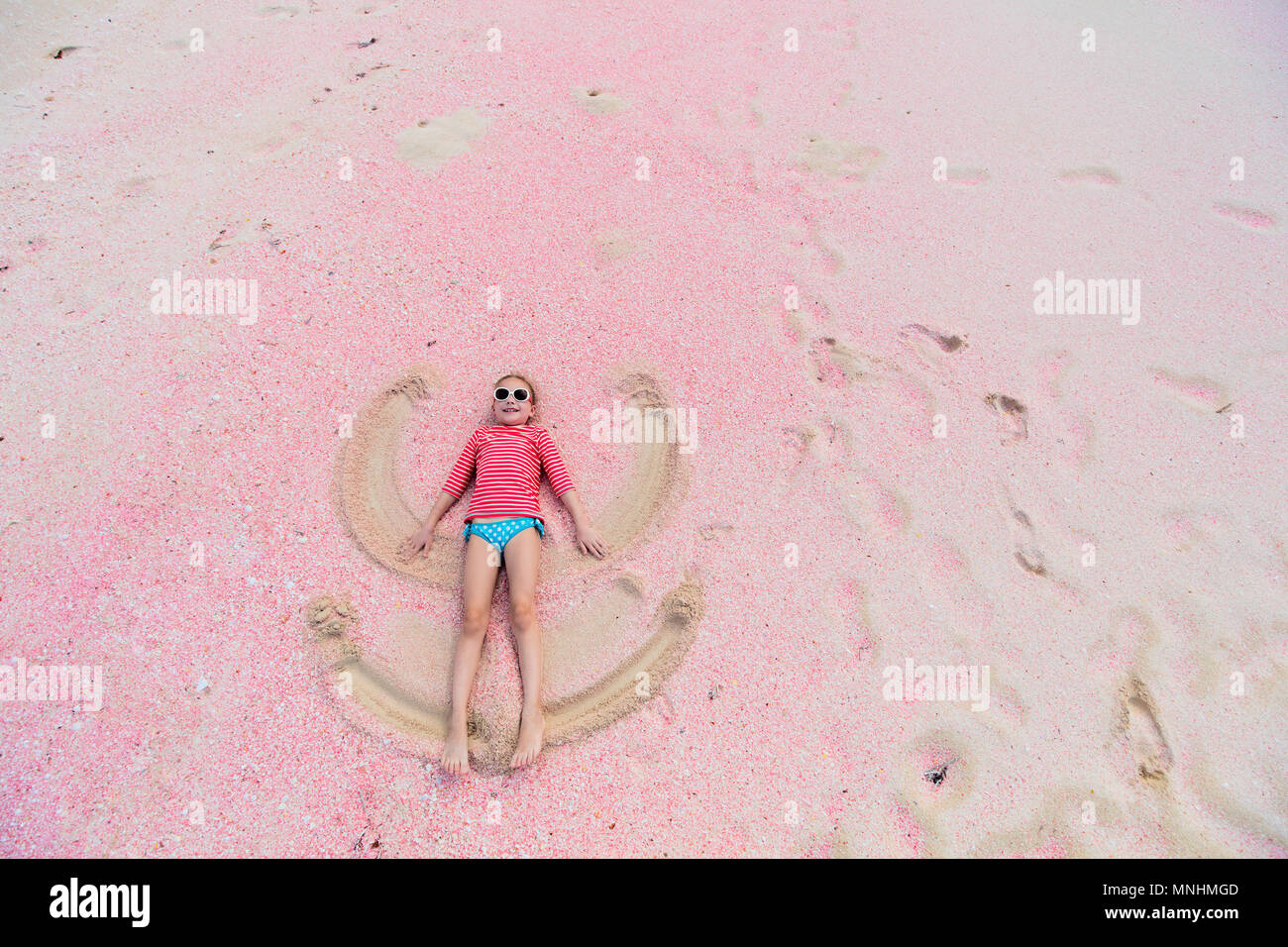 Above view of a little girl making sand angel on beautiful pink sand ...
