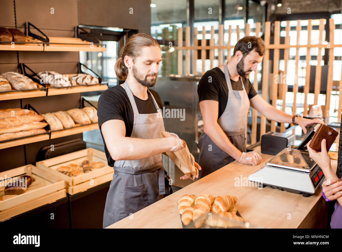 Two handsome sellers in uniform selling bread to a young woman client ...