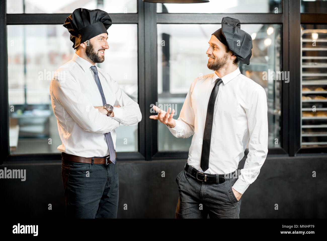 Two elegant bakers in white shirts and caps talking together in the ...