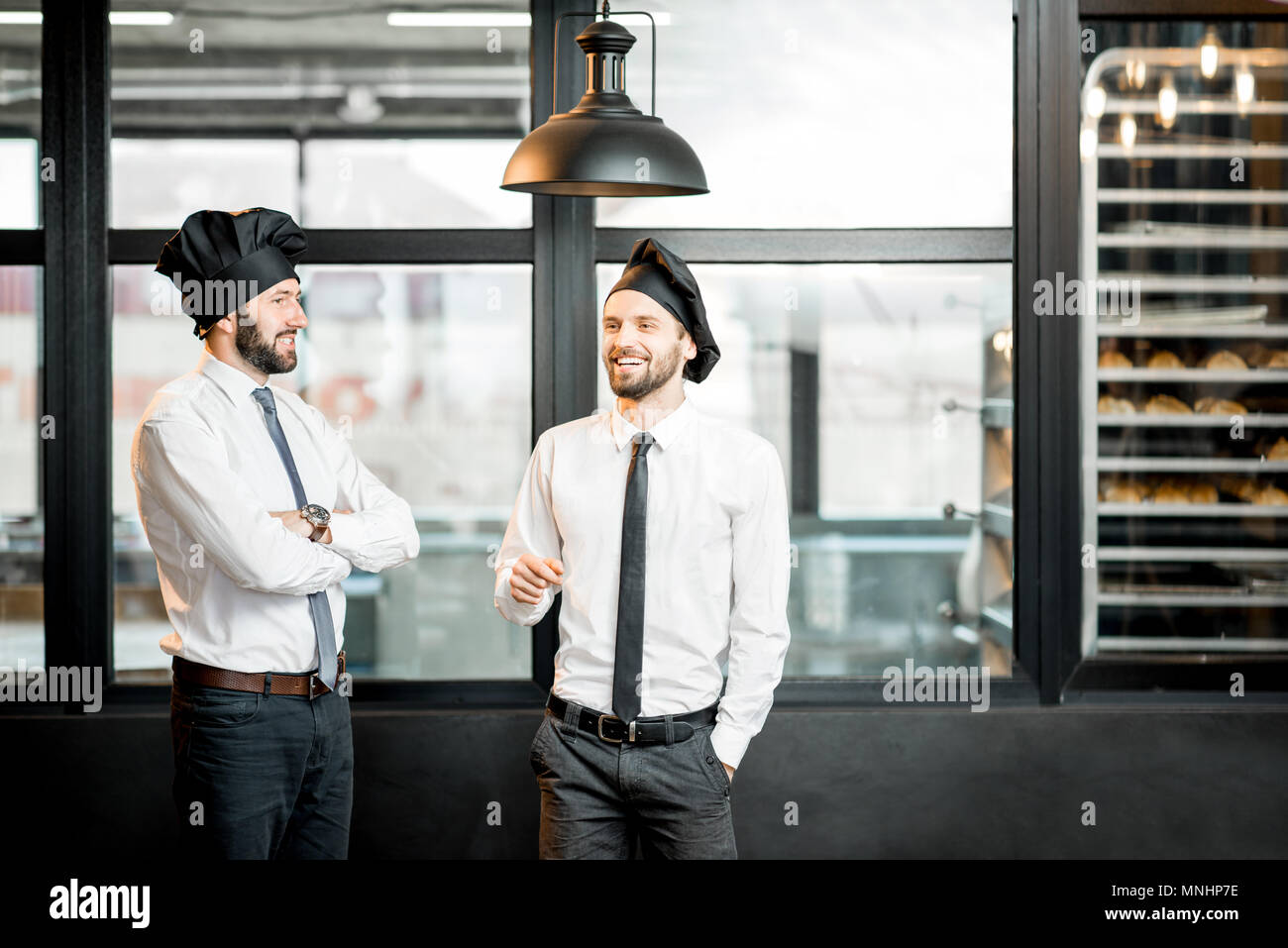 Two elegant bakers in white shirts and caps talking together in the ...