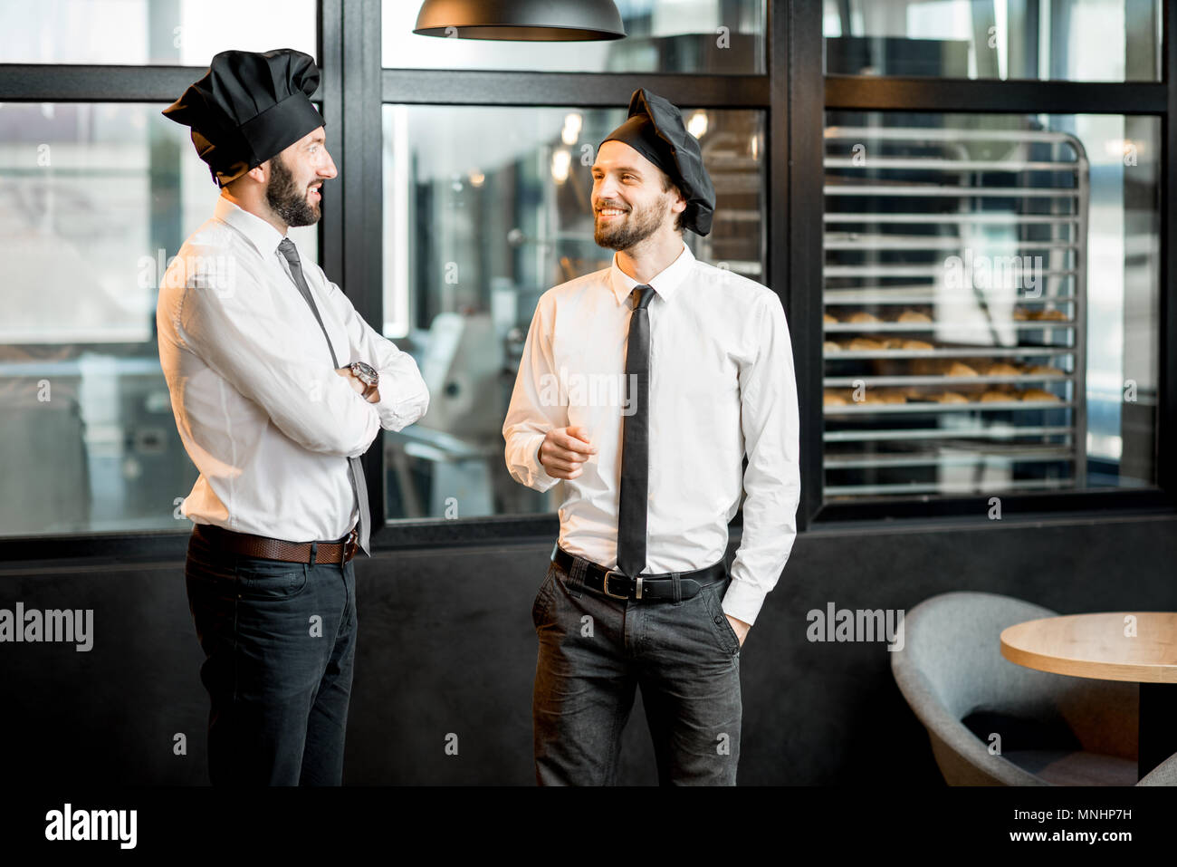 Two elegant bakers in white shirts and caps talking together in the ...