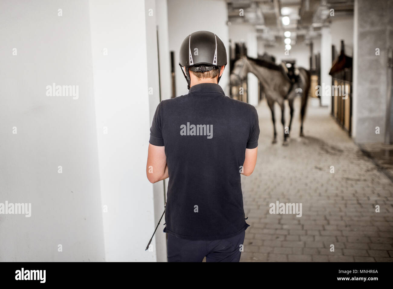 Man prepairing for horse riding standing back in the stable with horse ...