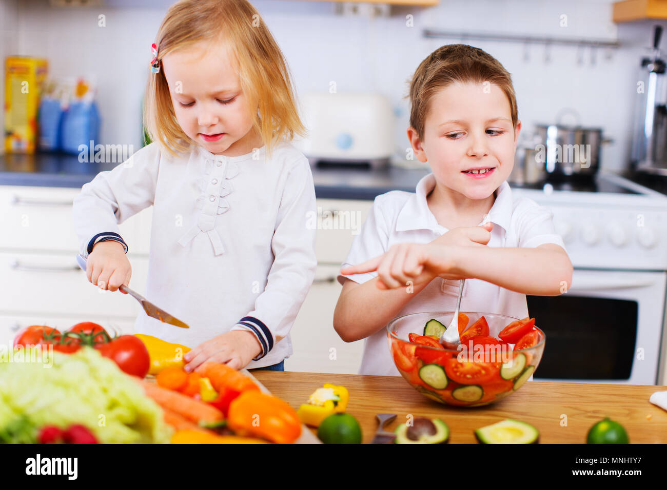 Two little kids helping at kitchen with salad making Stock Photo - Alamy