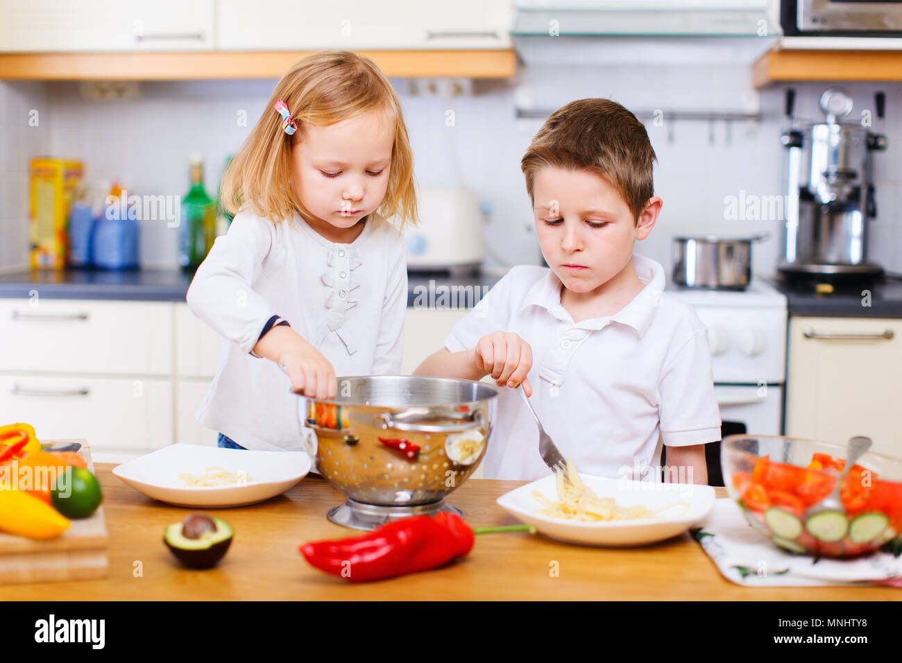Two little kids helping at kitchen with salad making Stock Photo - Alamy