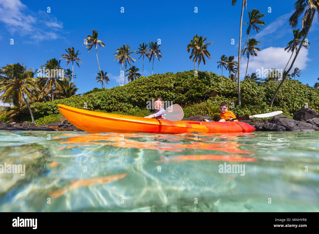 Kids enjoying paddling in colorful red kayak at tropical ocean water ...