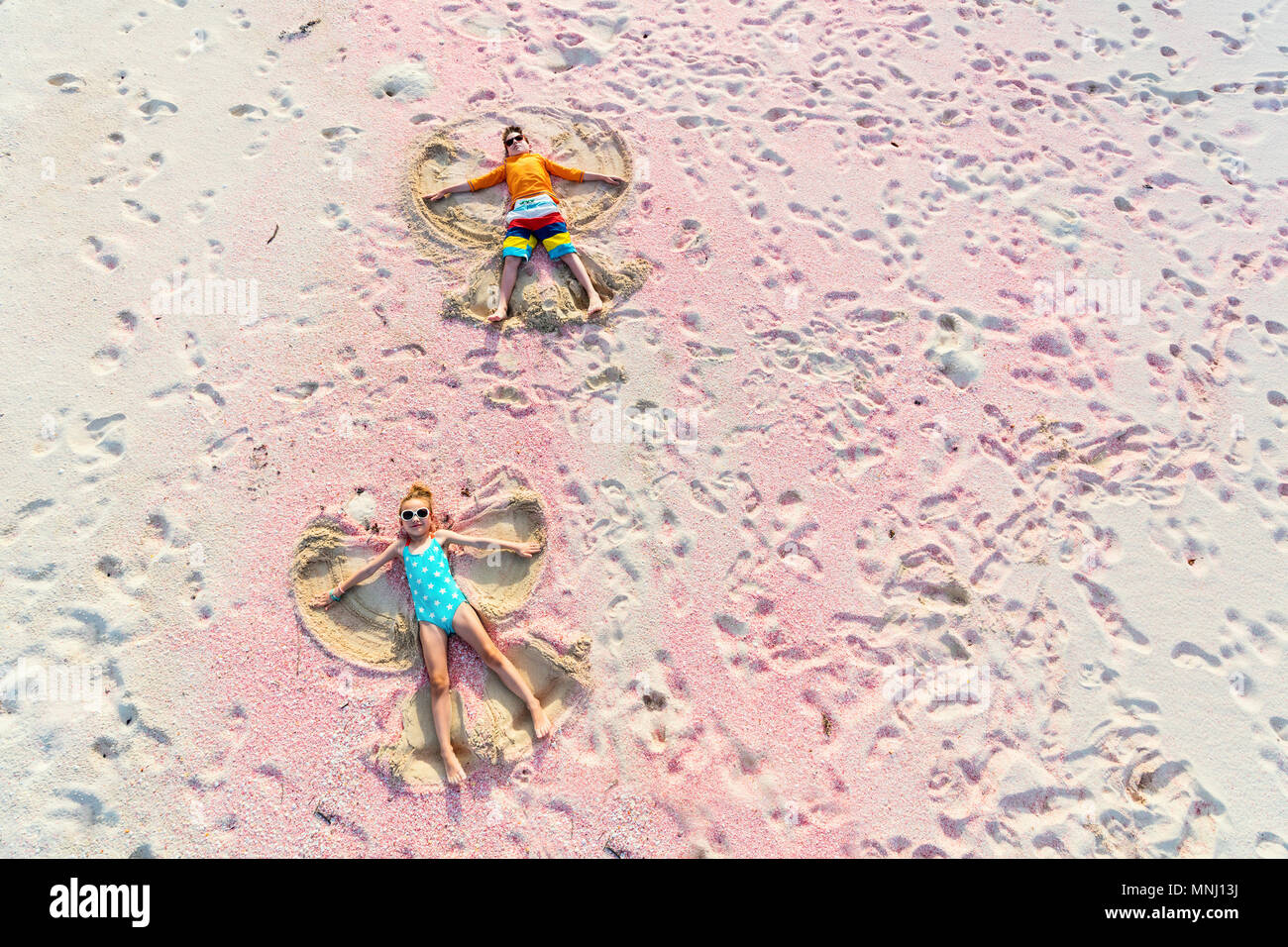Above view of kids making sand angels on beautiful pink sand beach at ...
