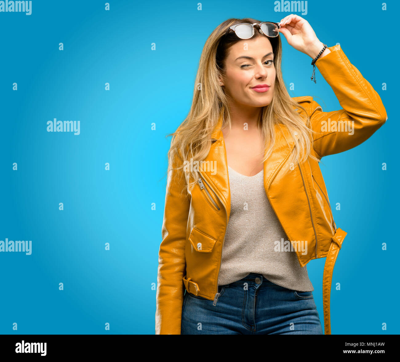 Beautiful young woman blinking eyes with happy gesture, blue background ...
