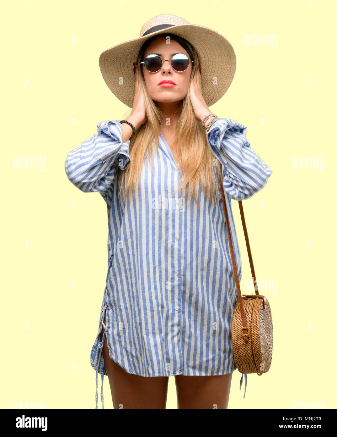 Young woman wearing sunglasses and summer hat covering ears ignoring ...