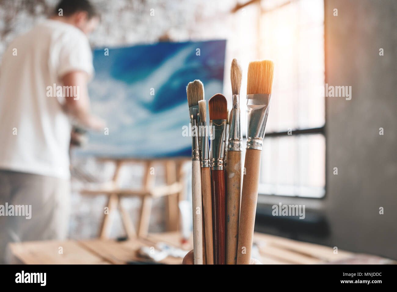 Man painter working in workshop in back of the canvas and drawing ...