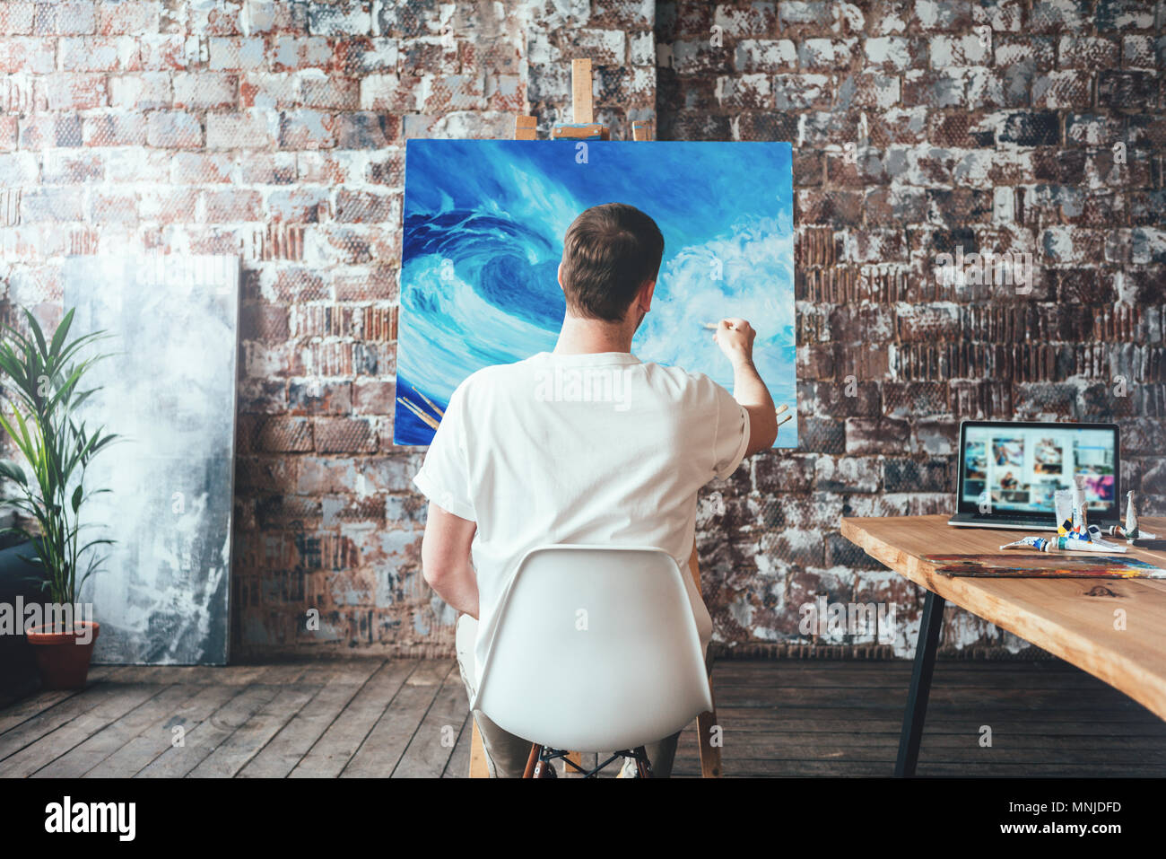 Man artist sitting on chair in front of canvas on easel and drawing ...