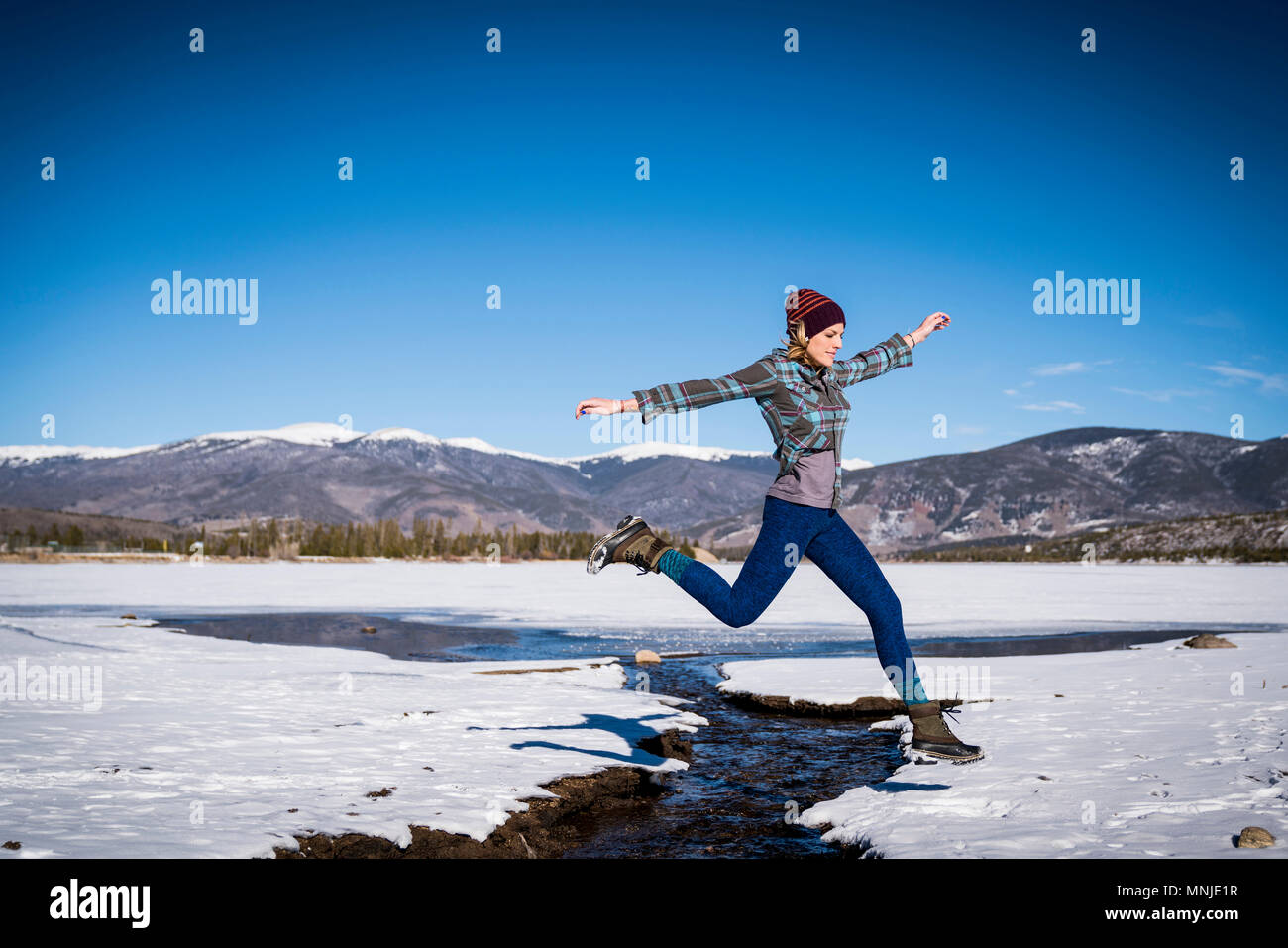 Woman jumping over stream in winter in snowy field Stock Photo - Alamy