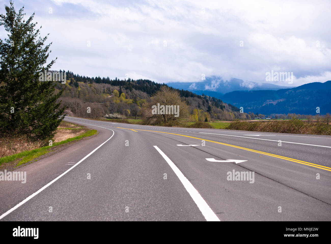 Wide multi-lane highway road with markings and arrows passes through ...