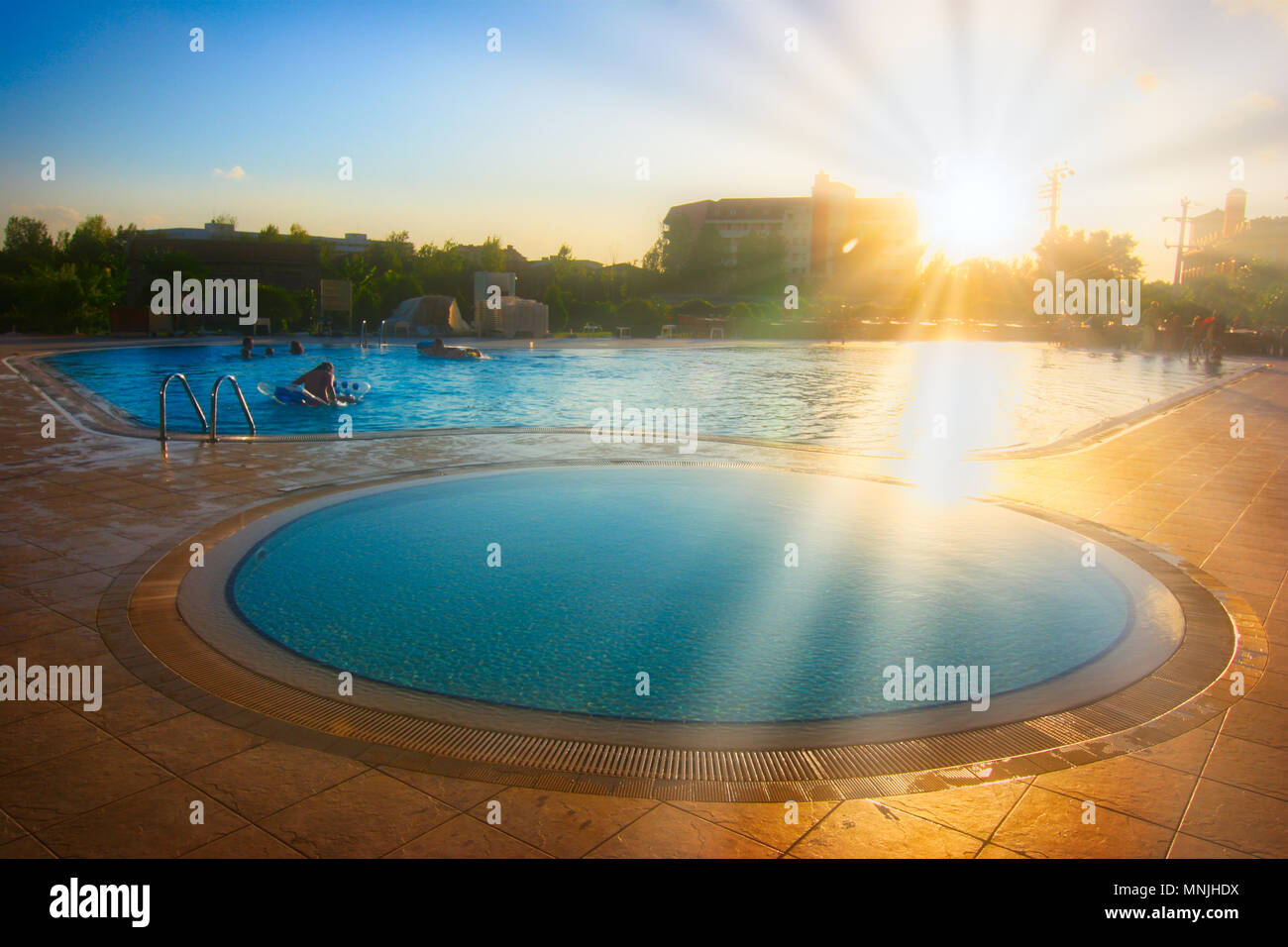 Beautiful sunset at a resort pool with bathing guests Stock Photo - Alamy