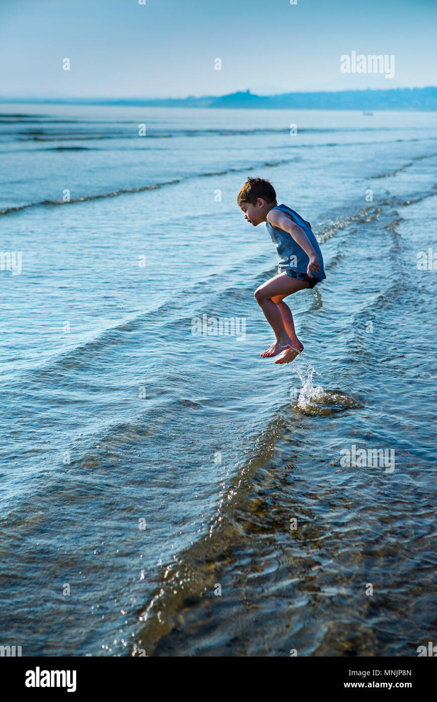 Young boy jumping over ocean waves, Cardigan Bay, North Wales, UK Stock ...