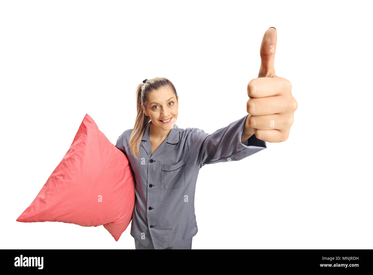 Young woman in pajamas holding a pillow and making a thumb up gesture ...