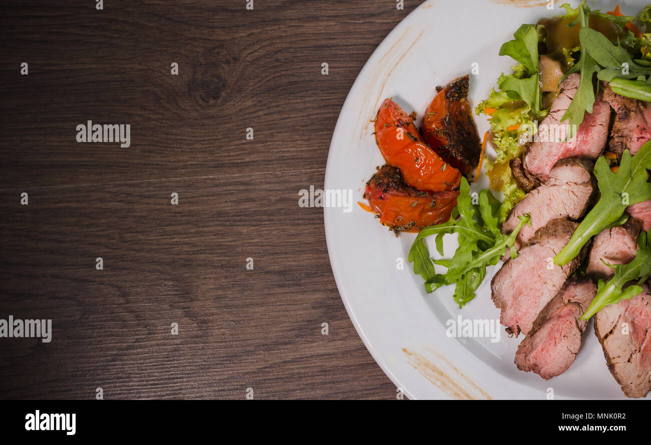 Roasted meat with blood in a cut with vegetables on a wooden background ...
