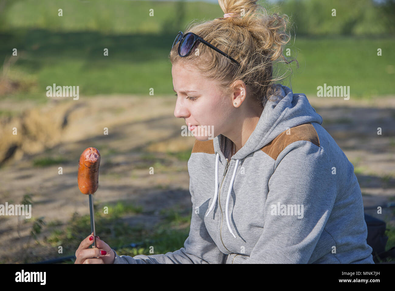 girl eating sausage from the grill, outdoors on the green grass camping ...