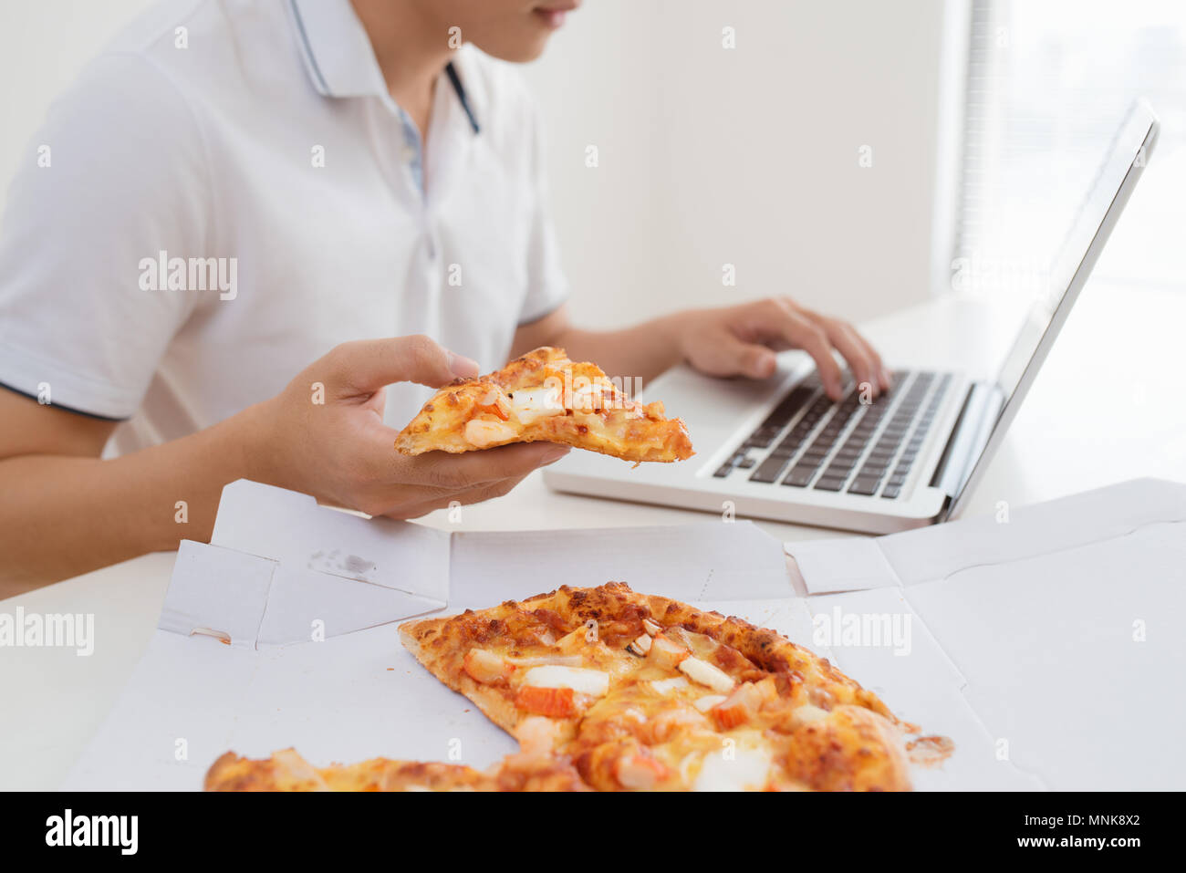 close up man hand eating pizza while working in laptop computer Stock ...
