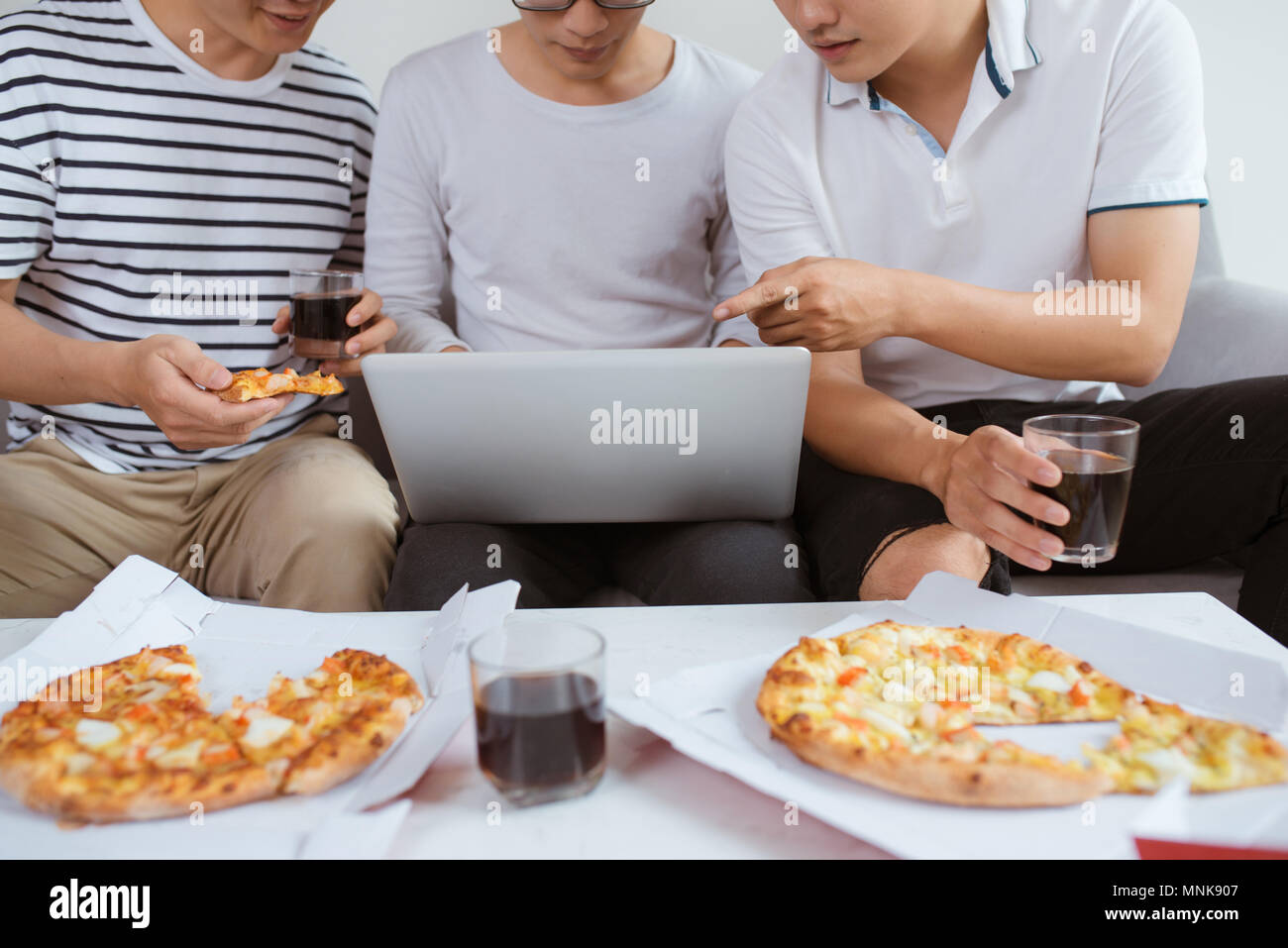 Joyful friends enjoying their pizza while sitting on couch at home ...