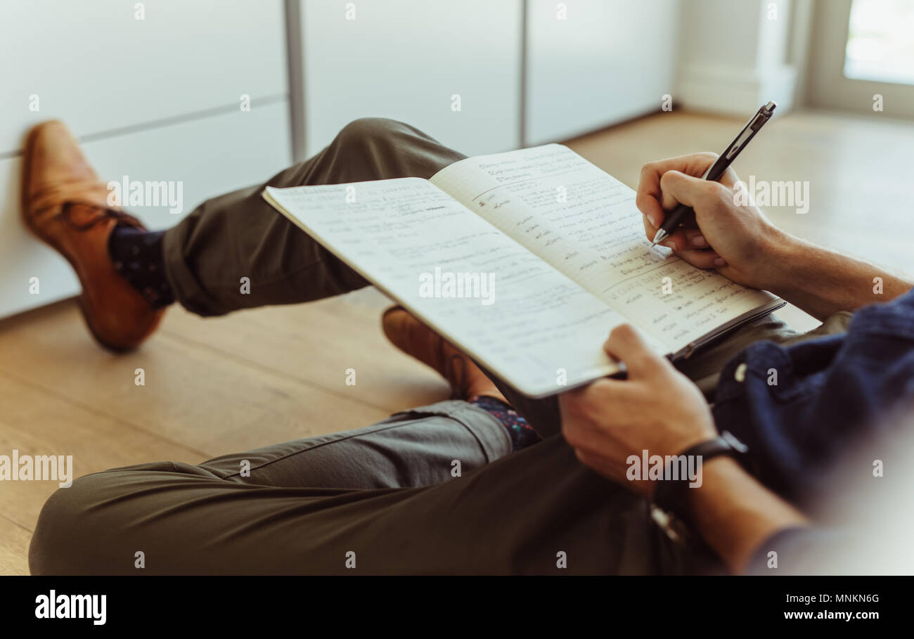 Side view of man sitting of floor at home and making notes in diary ...