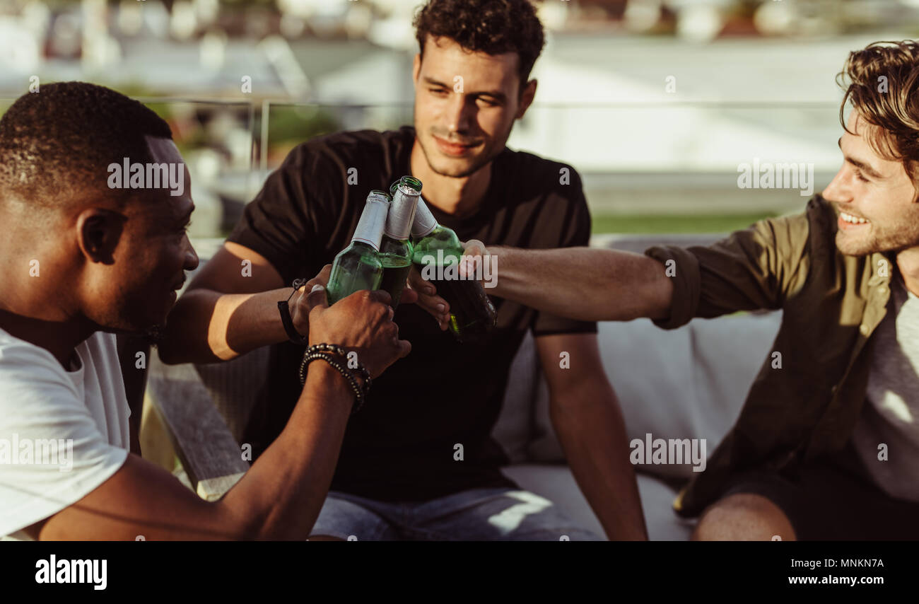 Three friends toasting their bottles of beer while having a party ...