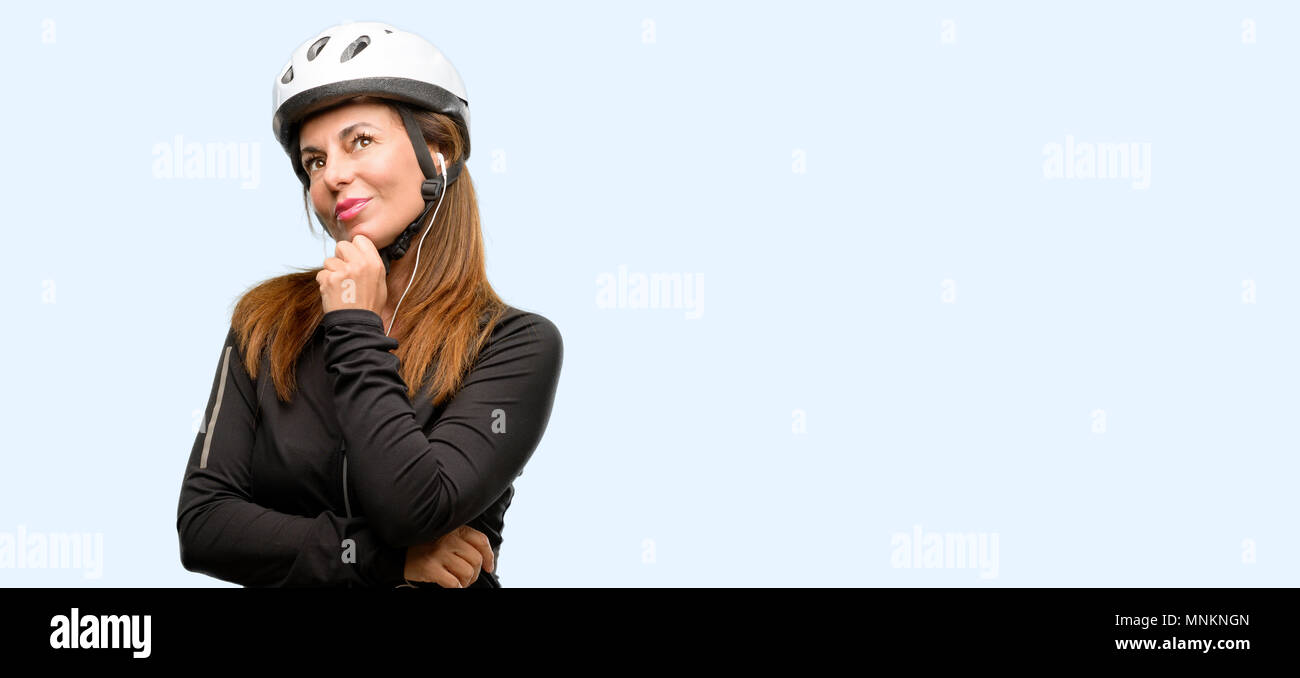Middle age cyclist woman using earphones thinking and looking up ...