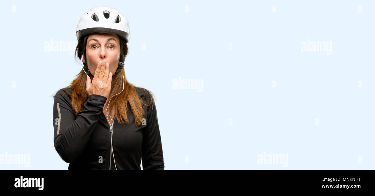 Middle age cyclist woman using earphones covers mouth in shock, looks ...