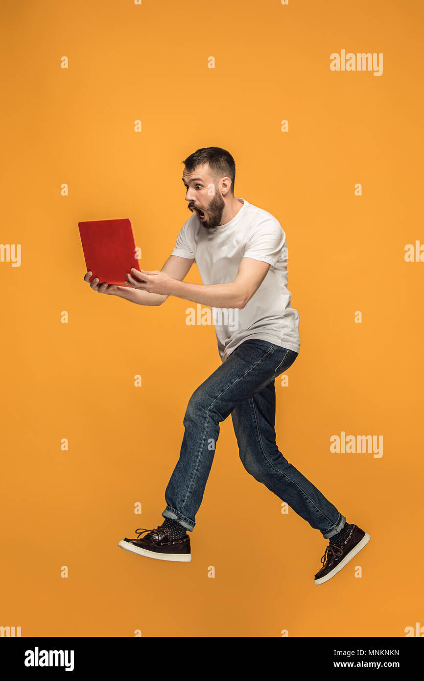 Image of young man over orange background using laptop computer while ...