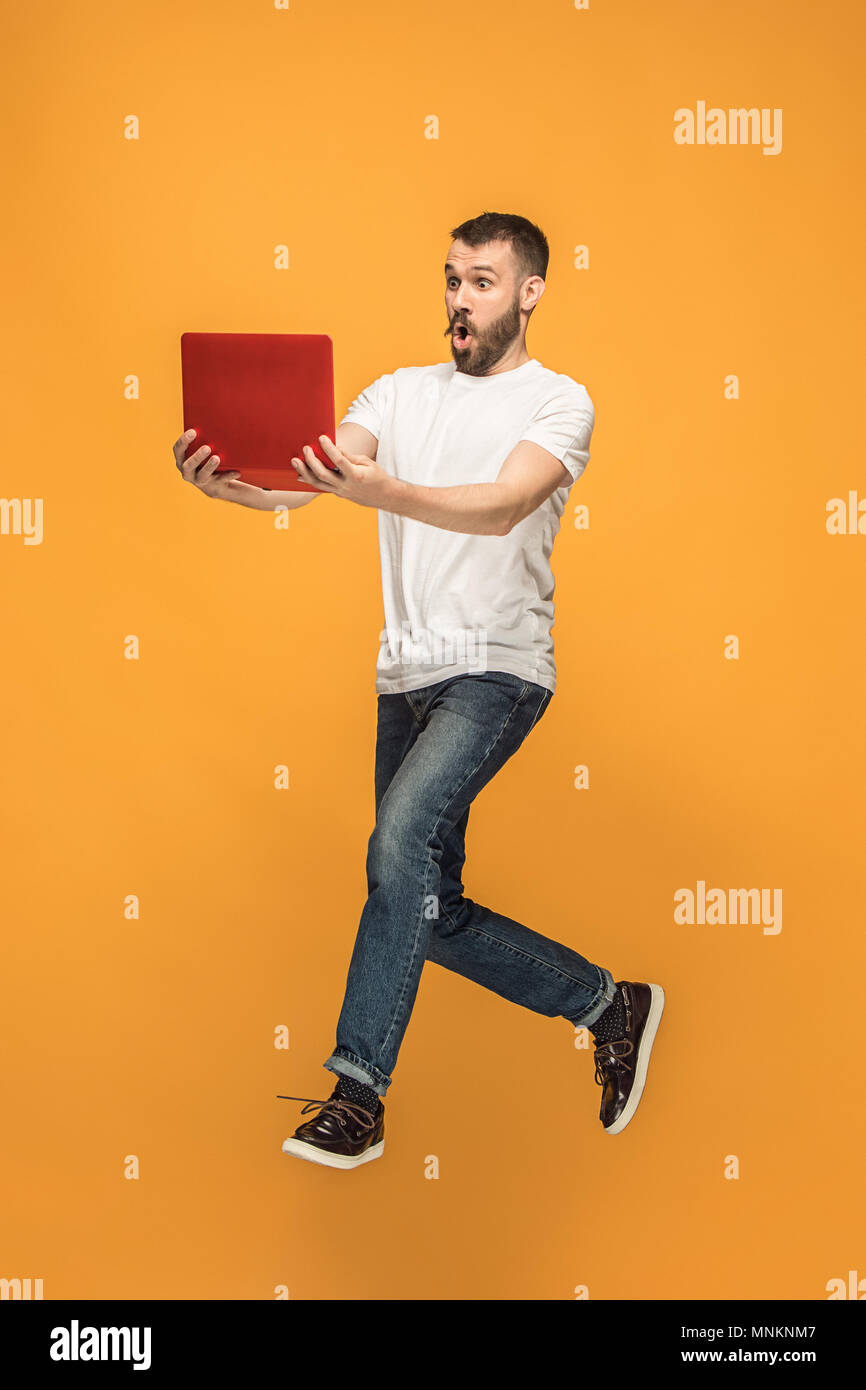 Image of young man over orange background using laptop computer while ...