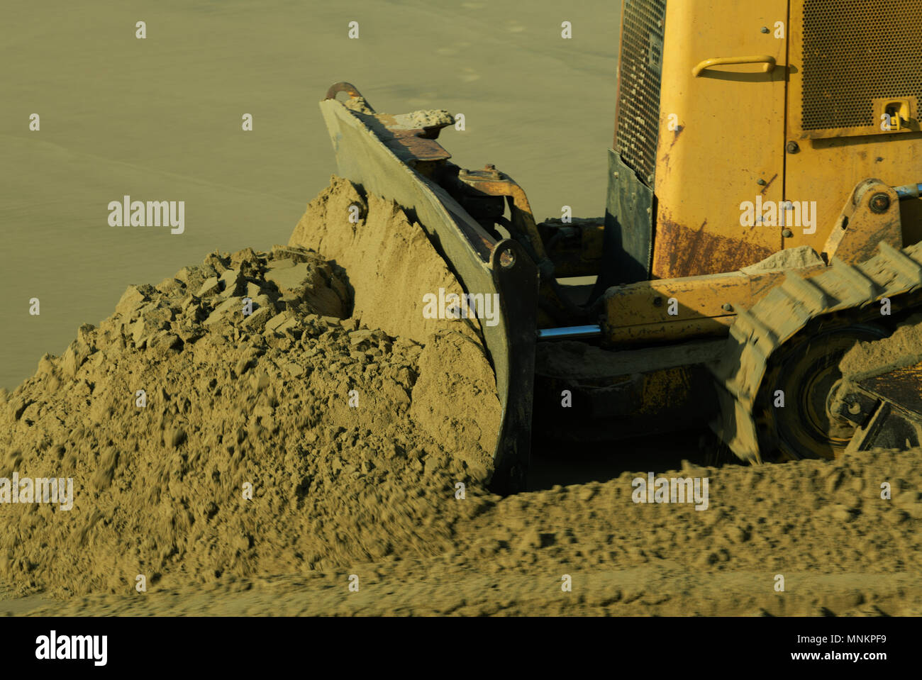 Close-up, blur, scraper blade of yellow bulldozer pushing beach sand ...