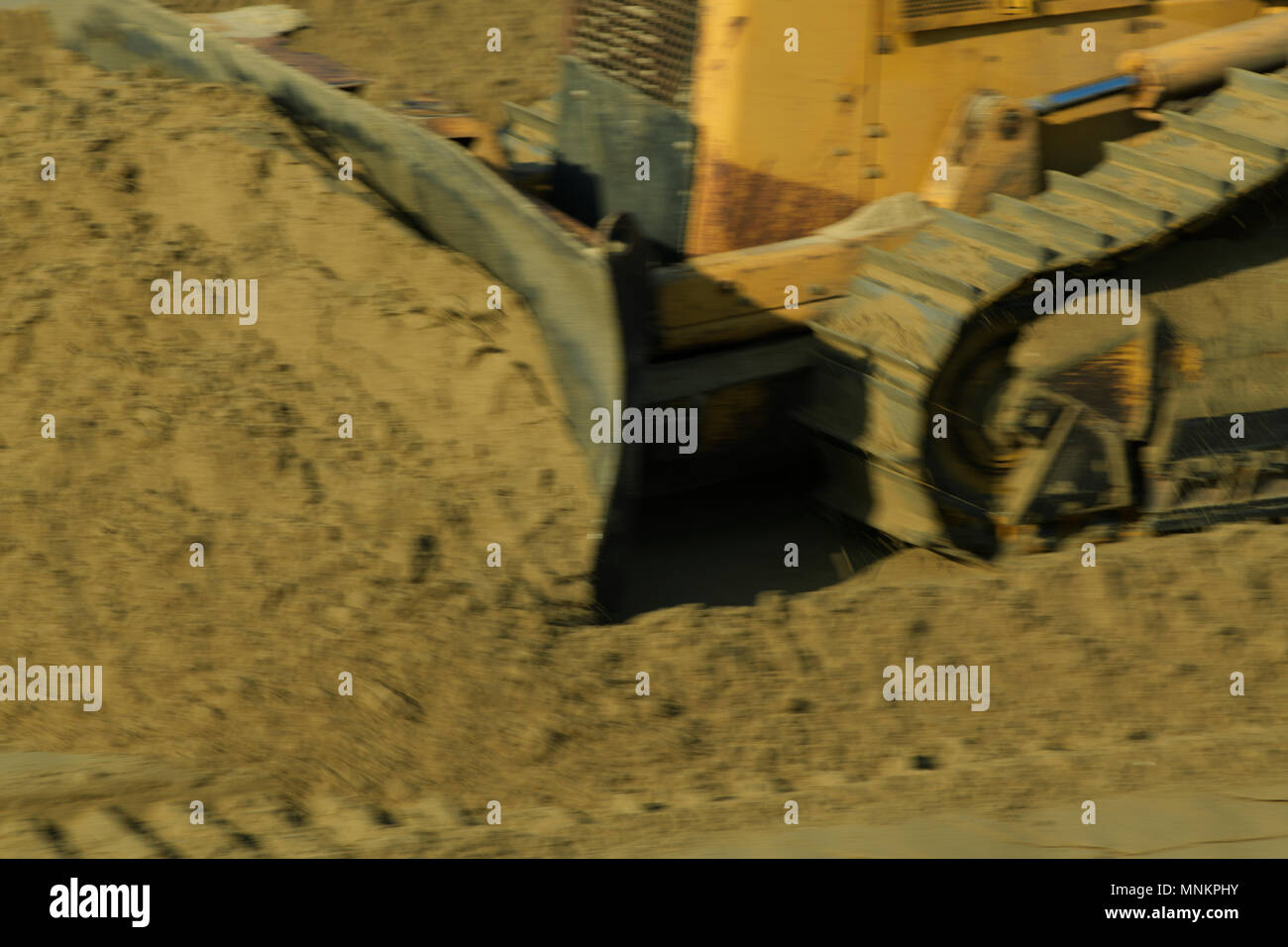 Blur, close-up, moving wet sand falling of scraper of yellow bulldozer ...