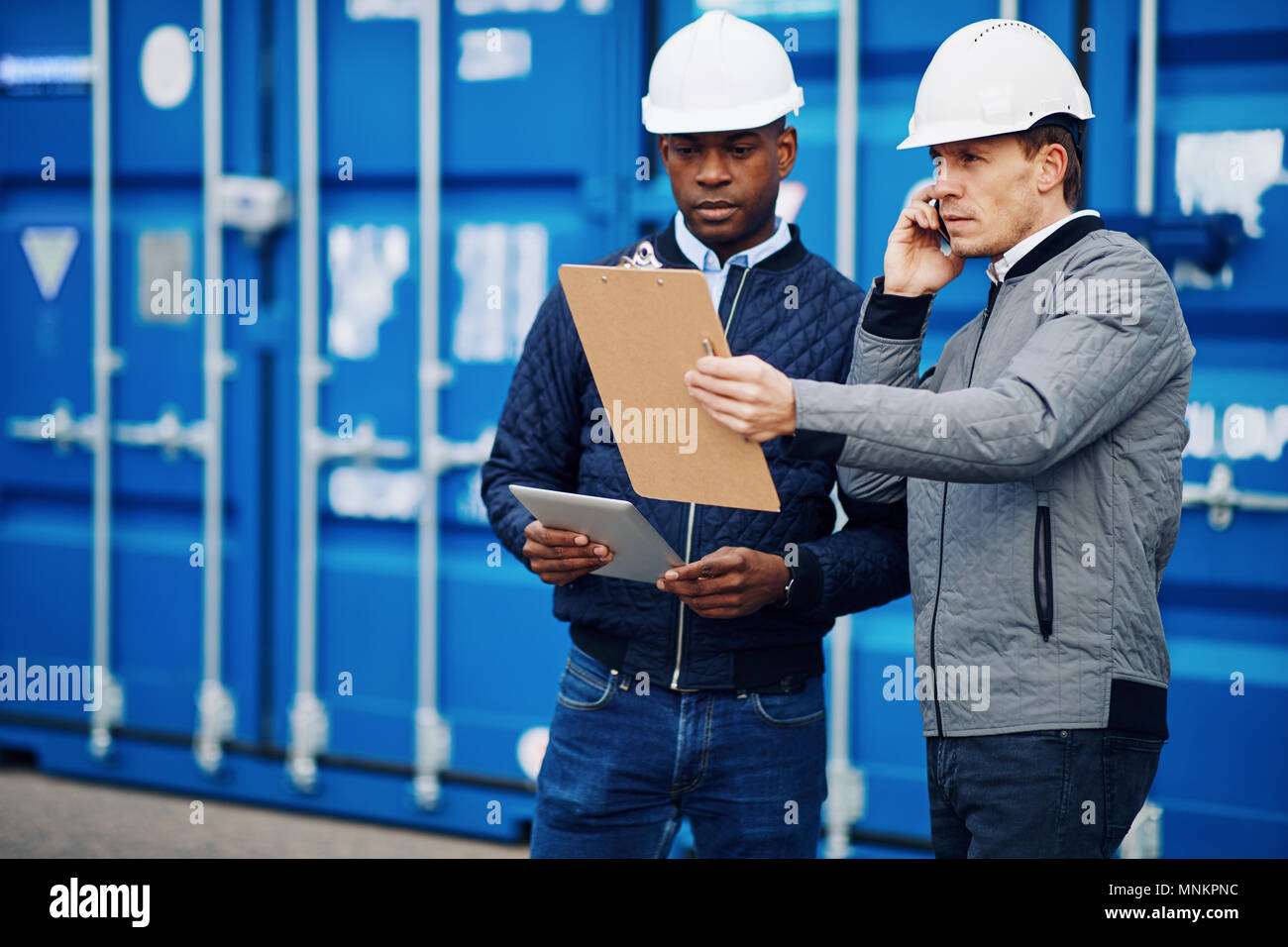 Freight manager standing with a colleague in a commercial shipping yard ...